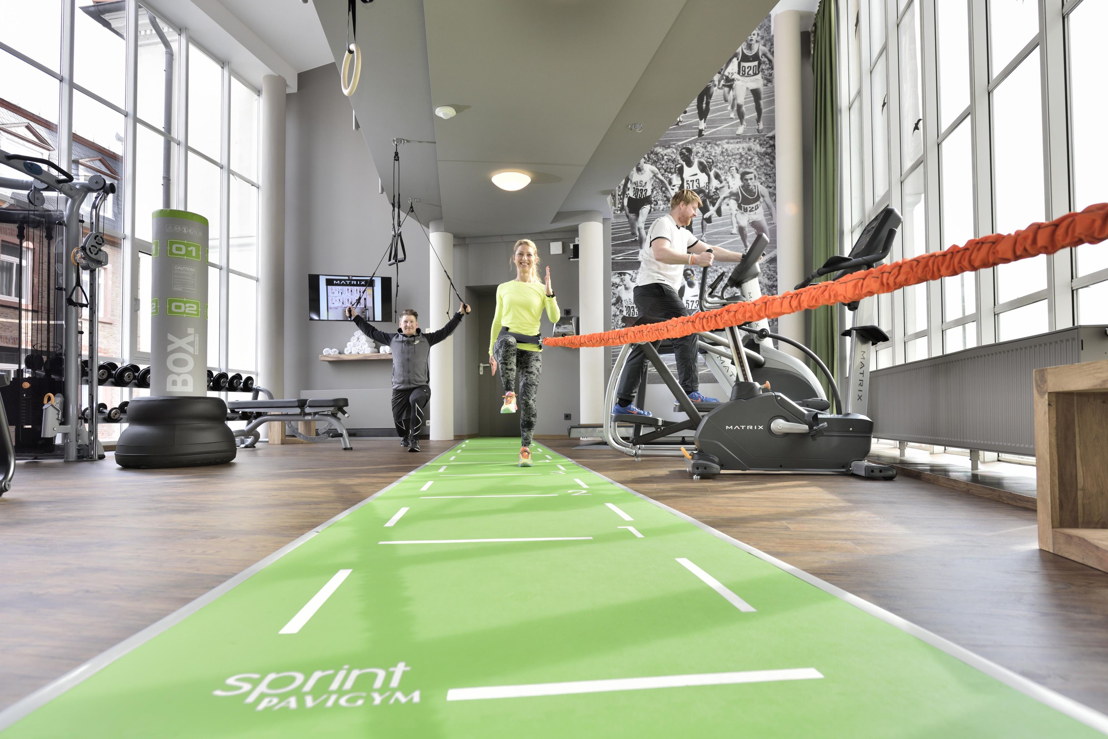 Academia com esteiras, máquina de remo e pista de corrida verde.