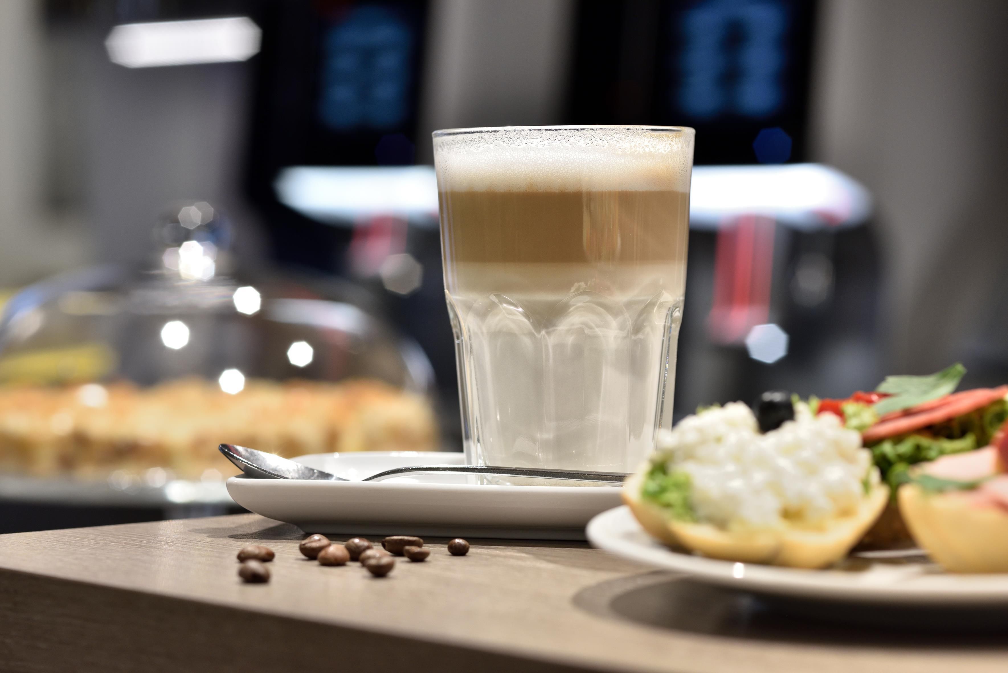 Um copo transparente com bebida e espuma, um prato com sanduíche e um prato com sobremesa sobre uma mesa de madeira.