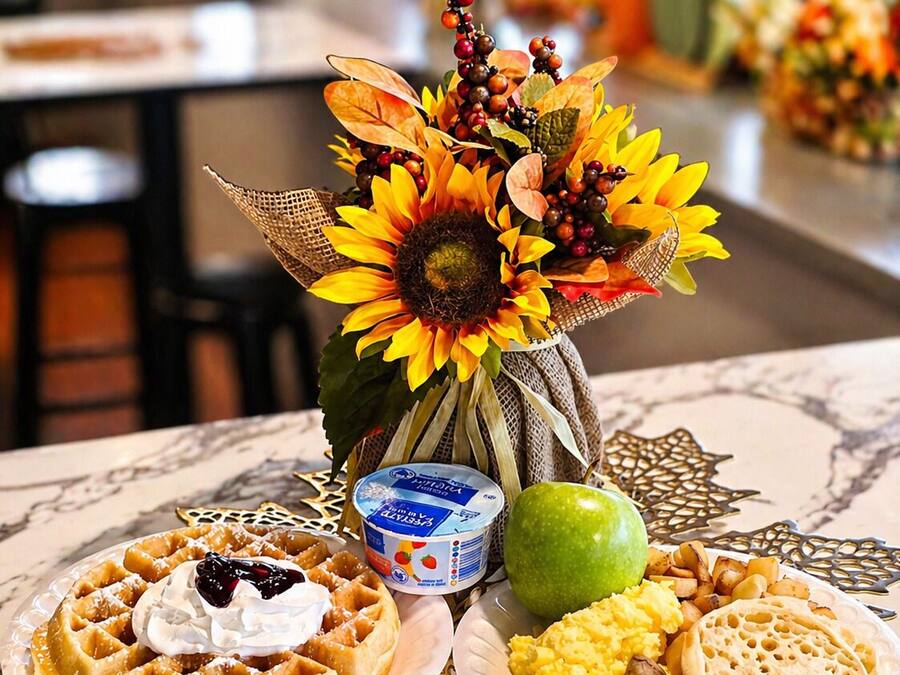 Uma mesa com waffles, uma maçã verde e um vaso decorativo com girassóis.