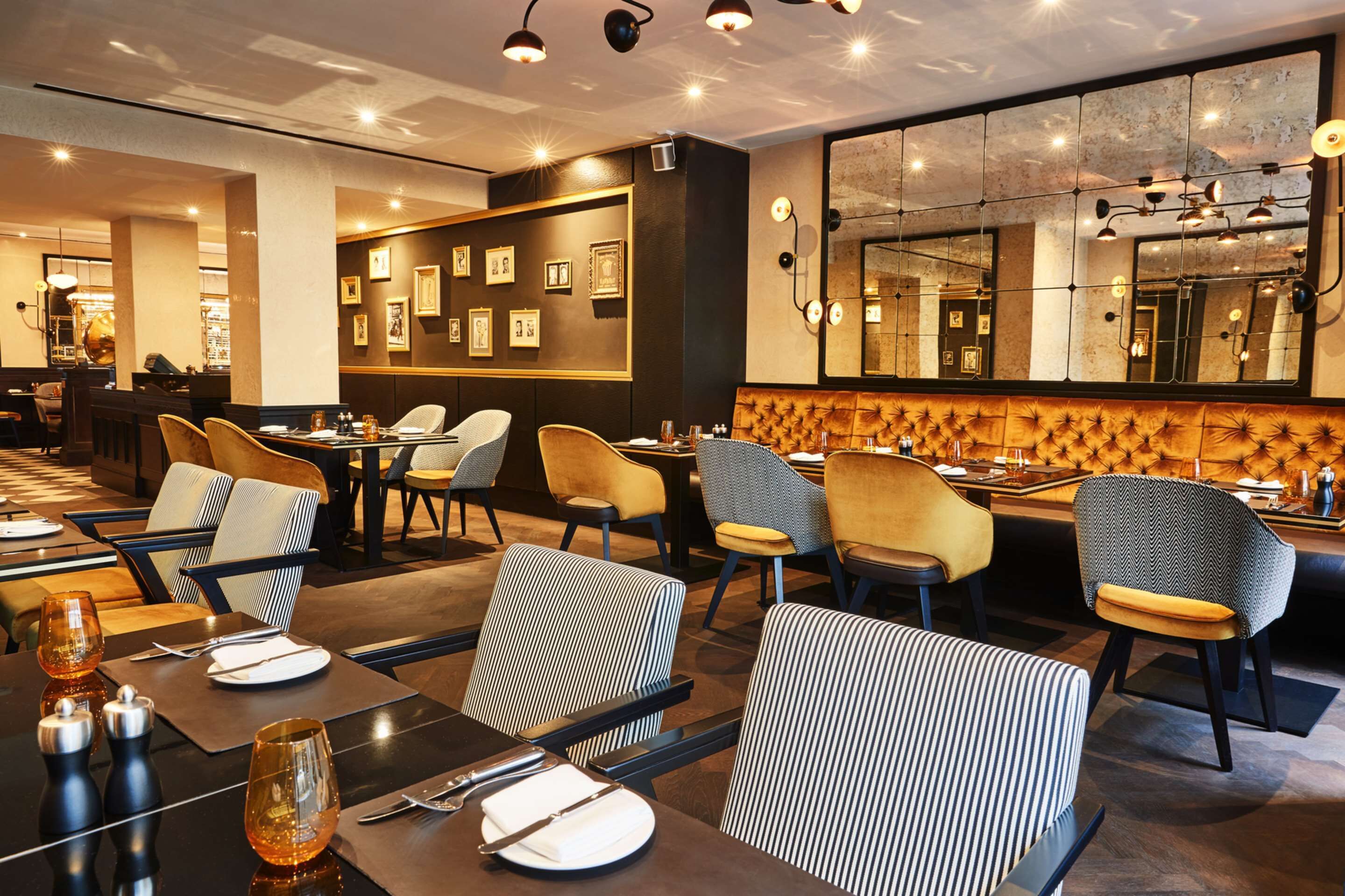 Restaurante com interior moderno, com cadeiras estofadas listradas e com capitonê, área de bar e quadros nas paredes.