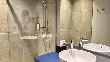 Uma casa de banho moderna com um espelho grande, duas sanitas, chuveiro com chuveiro manual e um porta-toalhas.