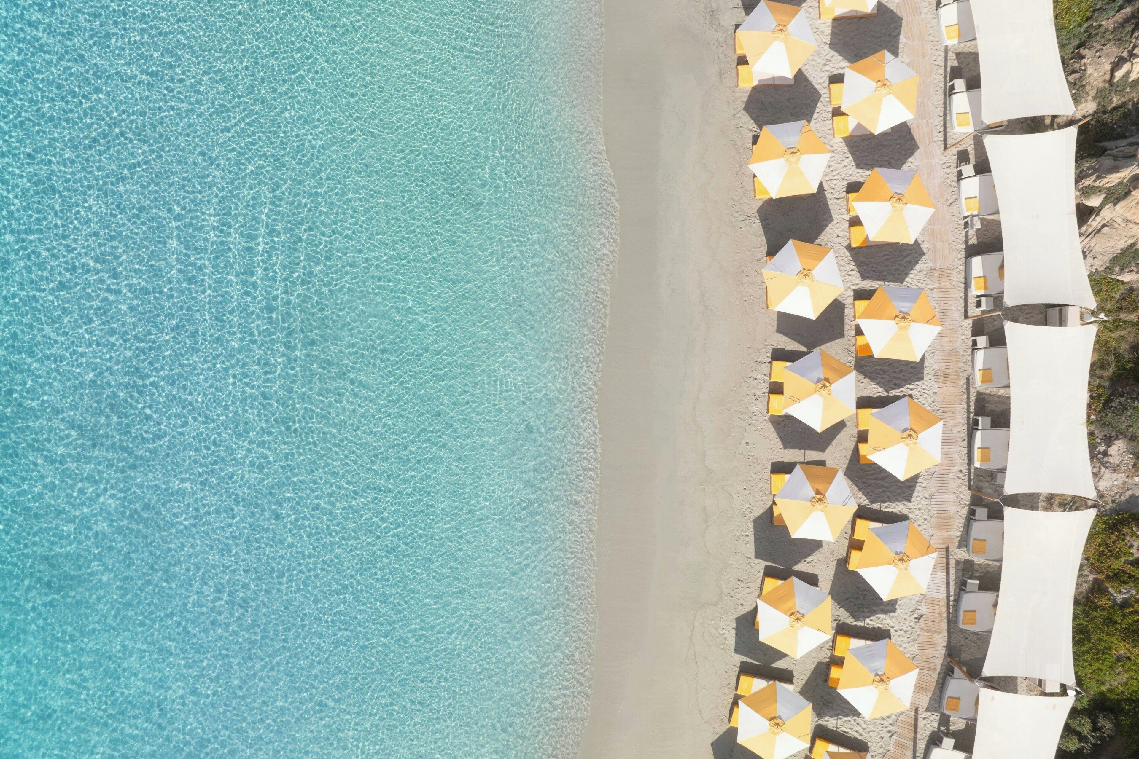 Vista aérea de uma praia com fileiras de guarda-sóis e cadeiras de praia, indicando um ambiente de resort.