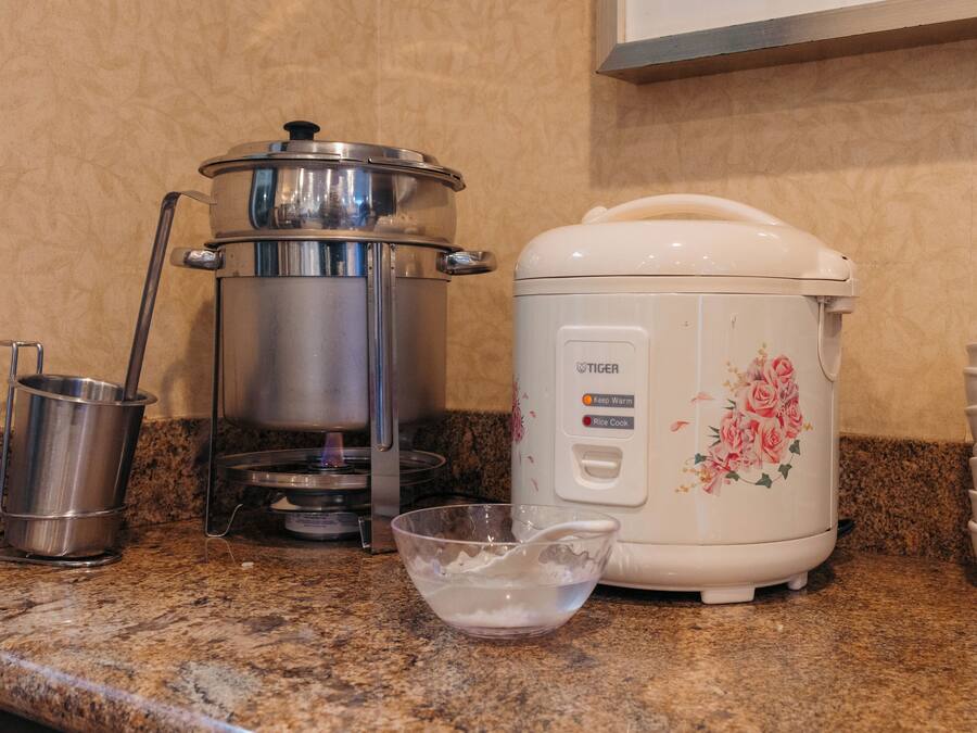 Uma bancada de cozinha com um cozedor de arroz, uma panela e uma tigela de vidro.