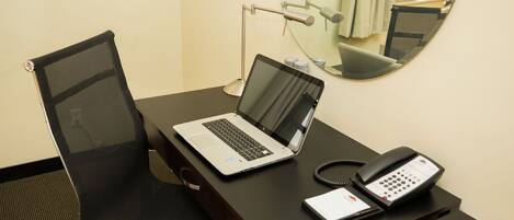 Quarto de hotel com uma escrivaninha, um laptop, um telefone e uma cadeira.