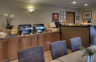 Espaço de pequeno-almoço de hotel com buffet, cadeiras de vime, balcão com bebidas e parede com certificados emoldurados.