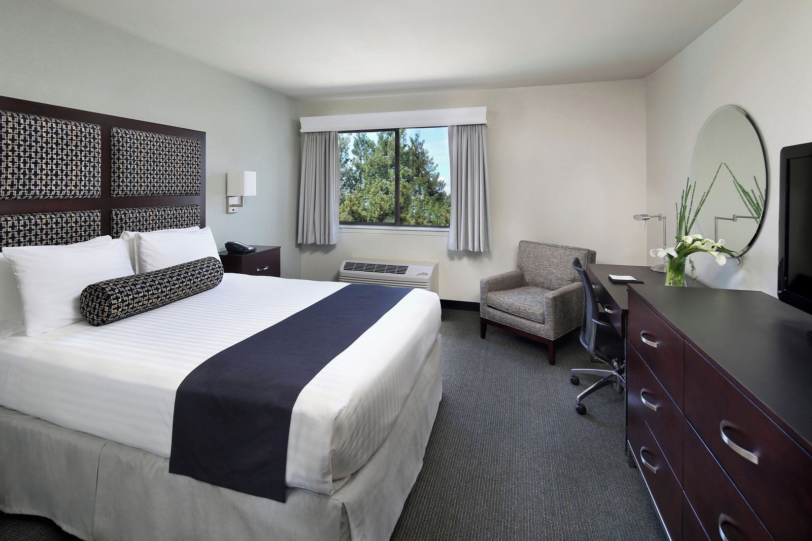 Quarto de hotel com uma cama grande, uma escrivaninha, uma cadeira e uma janela com cortinas.