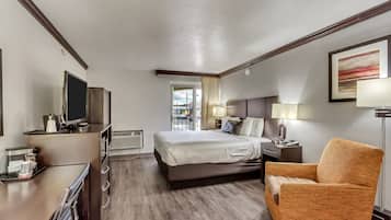 Quarto de hotel com cama, escrivaninha com cafeteira, televisão e uma cadeira.
