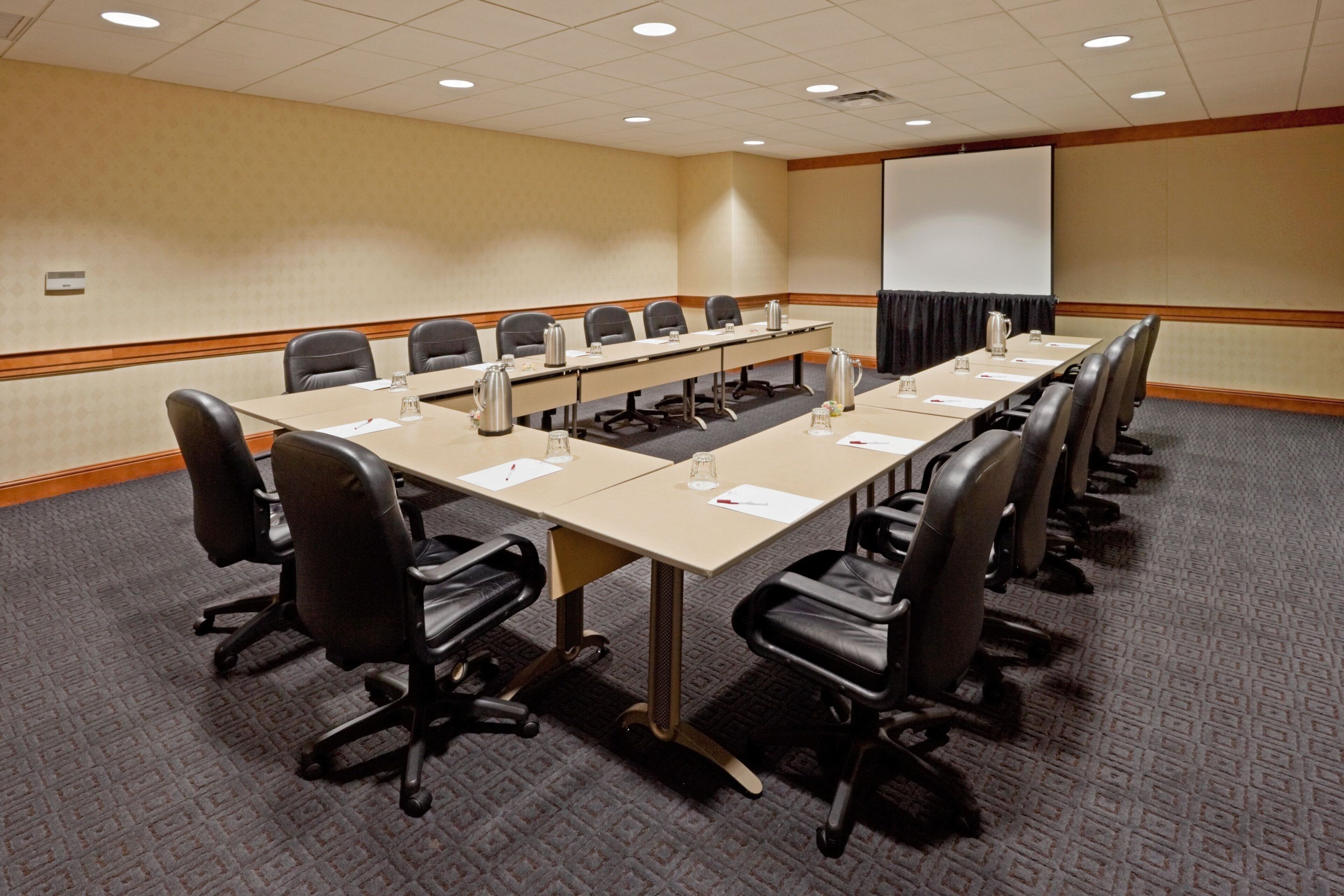Uma sala de conferências com uma mesa comprida, várias cadeiras e uma tela de projetor.