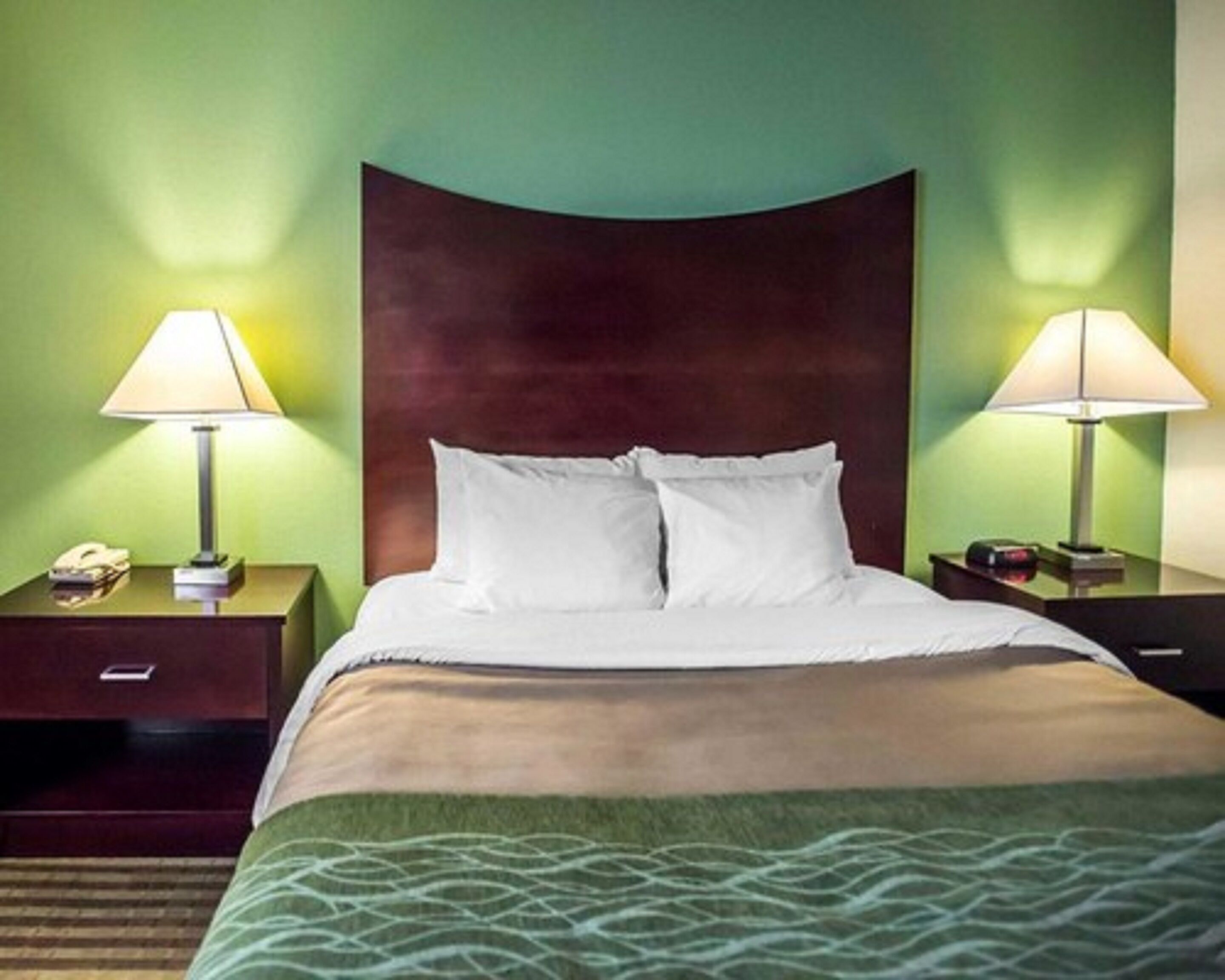 Quarto de hotel com uma cama, duas mesas de cabeceira e uma luminária em cada lado.
