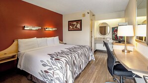 Quarto de hotel com cama, escrivaninha, cadeira, espelho e televisão.