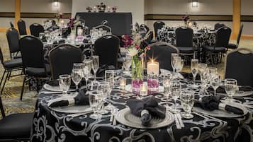 Uma sala de banquetes com mesas redondas dispostas para refeições, cada uma com talheres, copos e velas.