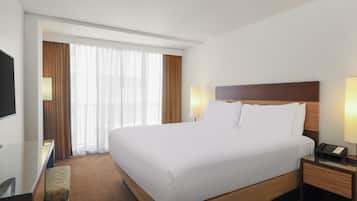 Quarto de hotel com cama grande, mesas de cabeceira, escrivaninha e televisão.