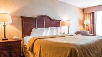 Quarto de hotel com uma cama grande, cabeceira de madeira, duas mesas de cabeceira com abajures, um criado-mudo e uma cadeira.