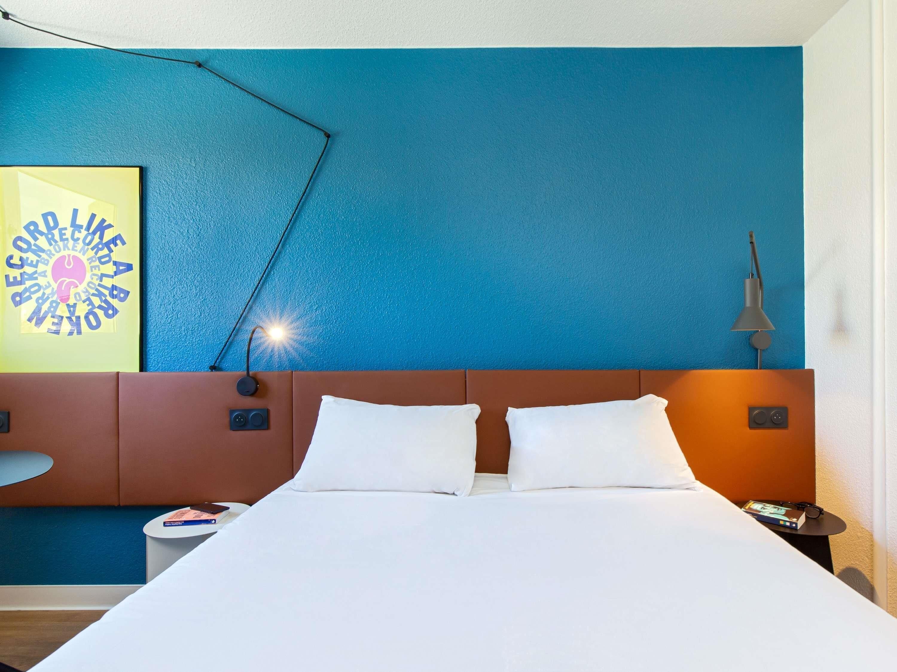 Quarto de hotel com cama, mesa de cabeceira, abajur e um poster na parede.