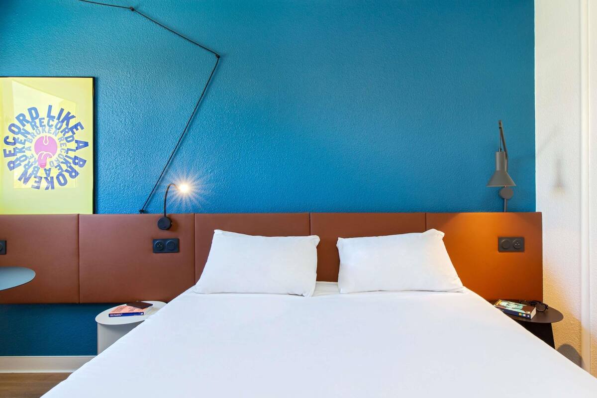 Quarto de hotel com cama, mesa de cabeceira, abajur e um poster na parede.