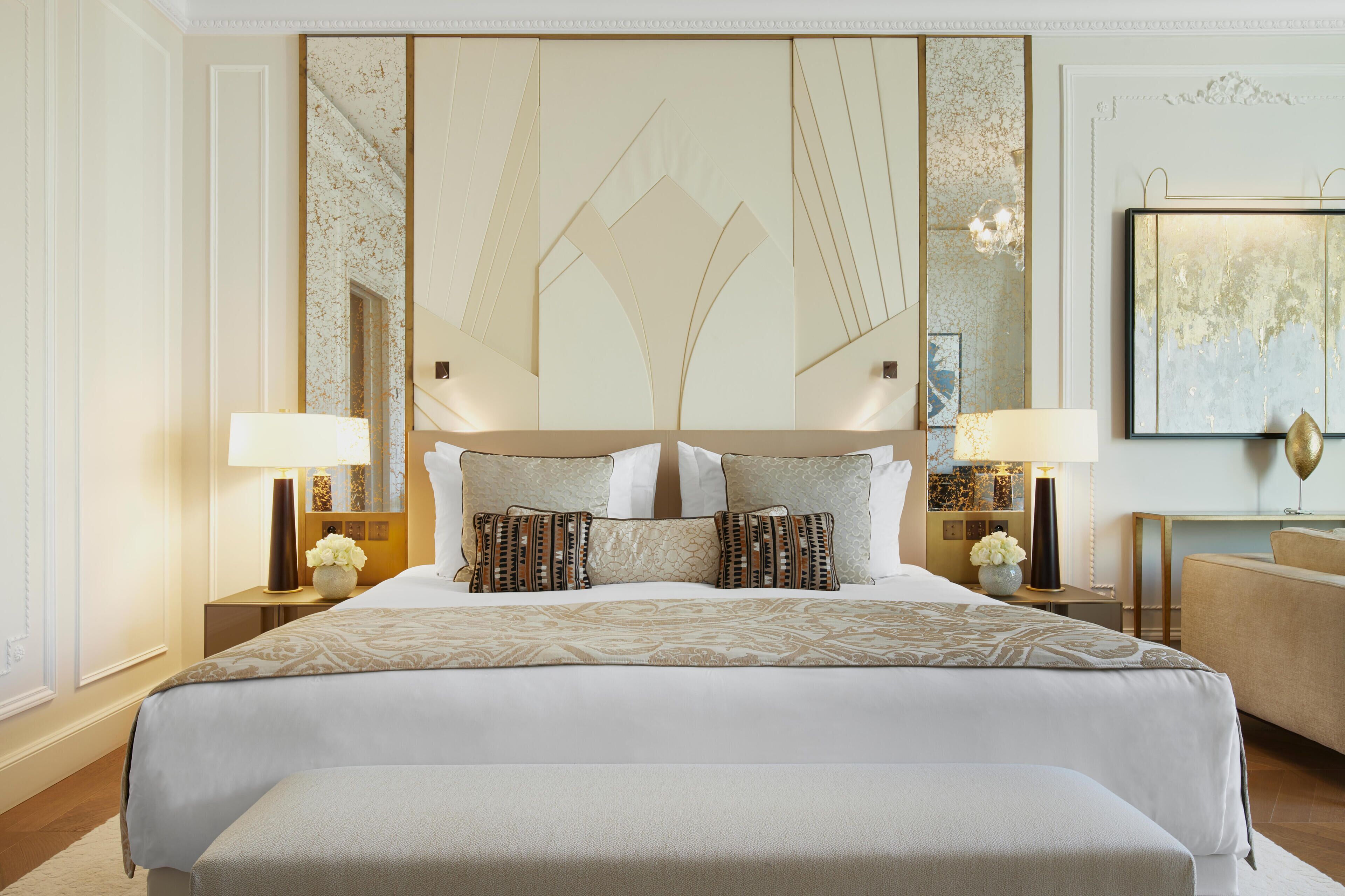 Quarto de hotel com uma cama grande, duas mesas de cabeceira com luminárias, um espelho grande e um quadro na parede.