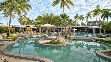 Área de piscina em resort, com espreguiçadeiras e guarda-sóis, cercada por palmeiras.