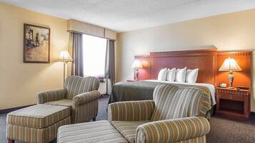 Quarto de hotel com uma cama, duas poltronas, uma mesinha, um criado-mudo e um abajur.