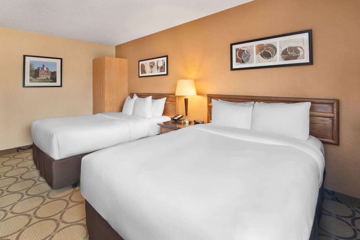 Quarto de hotel com duas camas, mesa de cabeceira com abajur e quadros nas paredes.