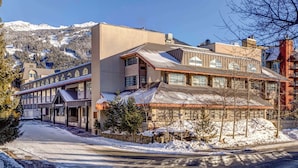 Hotel com estilo arquitetônico moderno, apresentando uma entrada destacada com galeria coberta e paisagem nevada ao fundo.