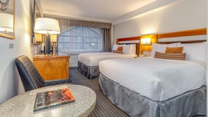 Quarto de hotel com duas camas, uma escrivaninha, uma cadeira, um abajur e uma janela com cortinas.