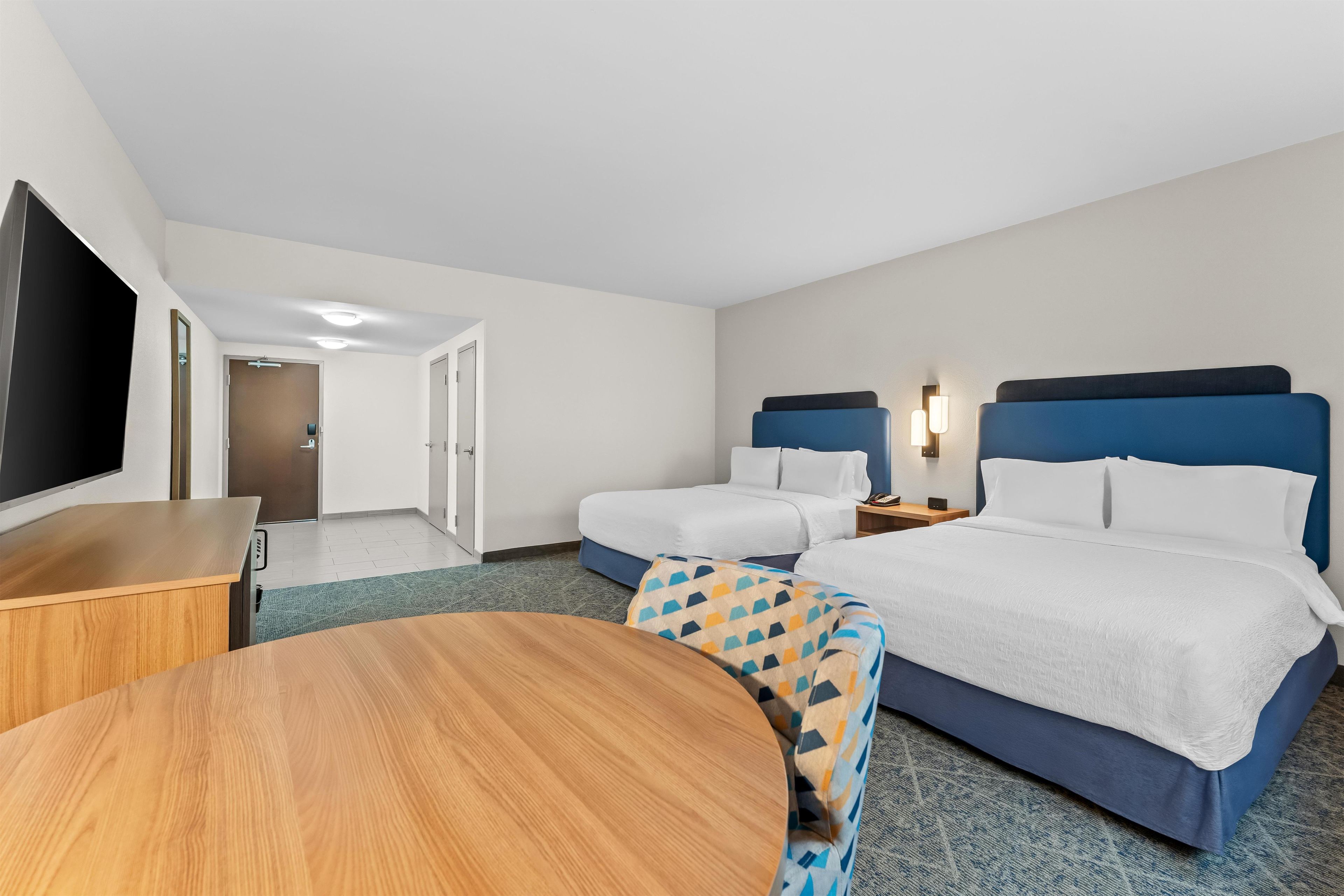Quarto de hotel com duas camas, televisão, escrivaninha e mesa redonda.