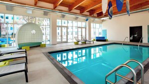 Piscina interna com teto de madeira, grandes janelas e espreguiçadeiras.