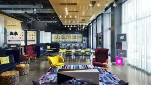 Espaço lounge moderno com assentos, bar e uma grande janela que oferece luz natural.