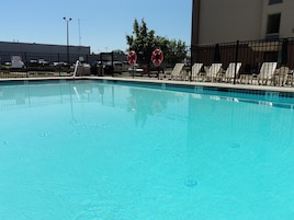 Piscina cercada por grade preta, cadeiras de espreguiçadeira e boias salva-vidas.
