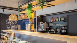 Uma área de bar com máquina de café, banquetas e prateleiras com garrafas de bebidas.