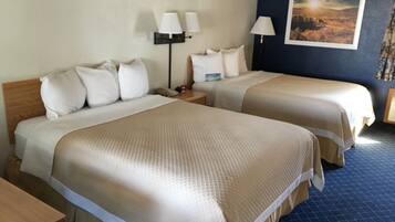 Quarto de hotel com duas camas, uma mesa de cabeceira, um abajur e um quadro na parede.