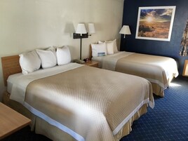 Quarto de hotel com duas camas, uma mesa de cabeceira, um abajur e um quadro na parede.
