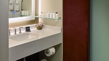 Casa de banho com um espelho grande, duas pias, um prateleira de vidro com produtos de higiene e um porta-toalhas com toalhas dobradas.