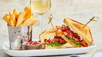 Um prato com um sanduíche grelhado, um copo de vinho branco e um recipiente com batatas fritas.