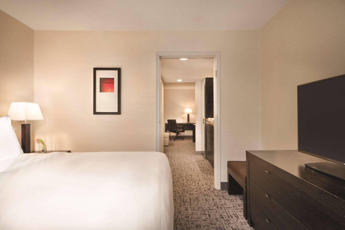 Quarto de hotel com cama, escrivaninha, cadeira, cômoda e televisão.
