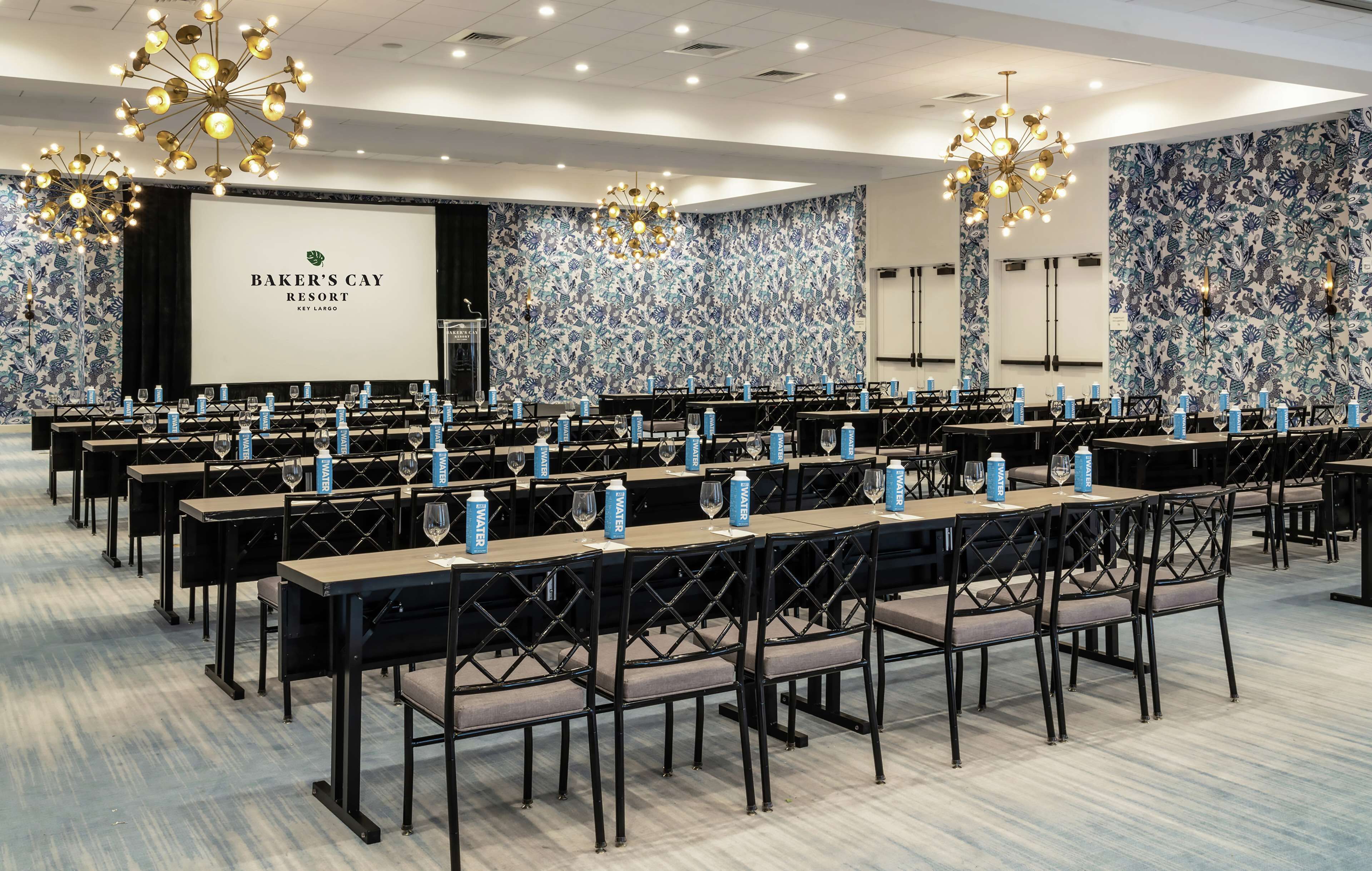 Uma sala de conferências no Baker's Cay Resort, com várias mesas, cadeiras e uma tela grande exibindo o nome do resort.
