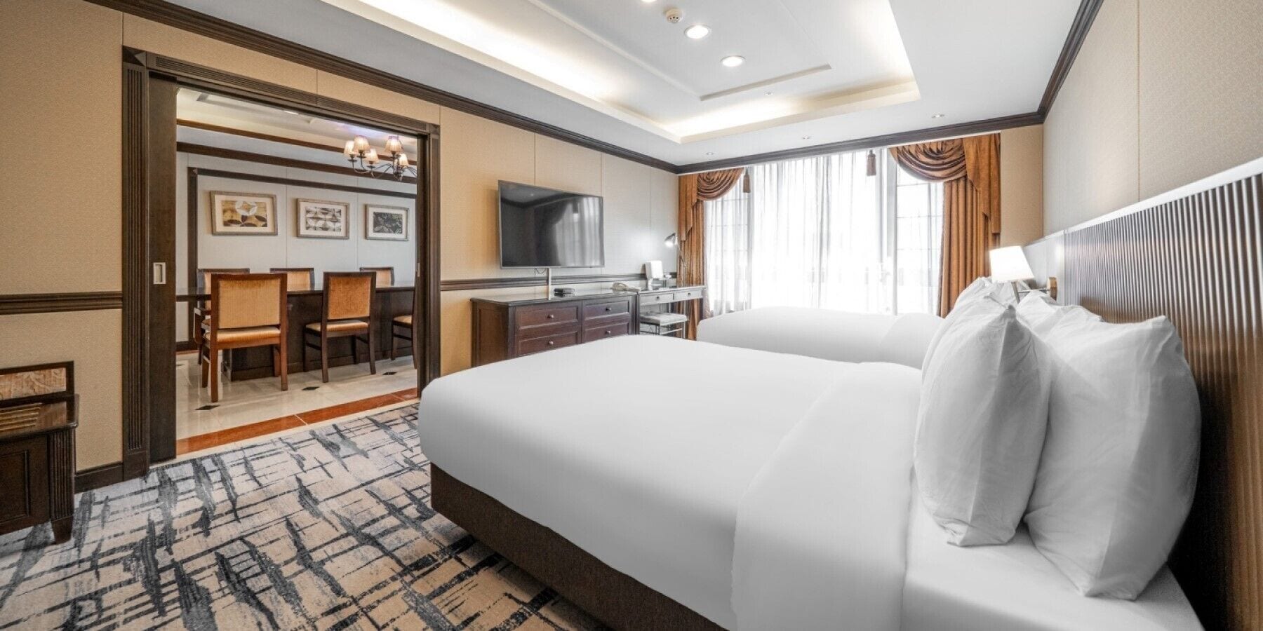 Quarto de hotel com uma cama grande, uma escrivaninha, uma cadeira, uma televisão e vista para o exterior.