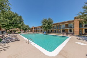 Piscina cercada por espreguiçadeiras e um edifício com várias varandas.