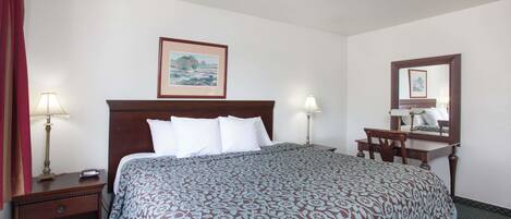 Quarto de hotel com uma cama grande, duas luminárias de cabeceira, uma mesa de cabeceira de madeira, uma escrivaninha com cadeira e um espelho.