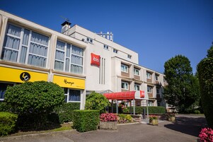 Um hotel com a placa vermelha 'ibis', uma placa amarela 'Camping' e um toldo vermelho sobre a entrada.