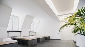 Um spa moderno com piso de pedra escura, uma grande palmeira em vaso e uma área de recepção com janela.