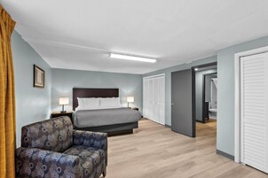 Quarto de hotel com uma cama, luminárias de cabeceira, uma poltrona estampada, um guarda-roupa e uma porta que dá para o banheiro.