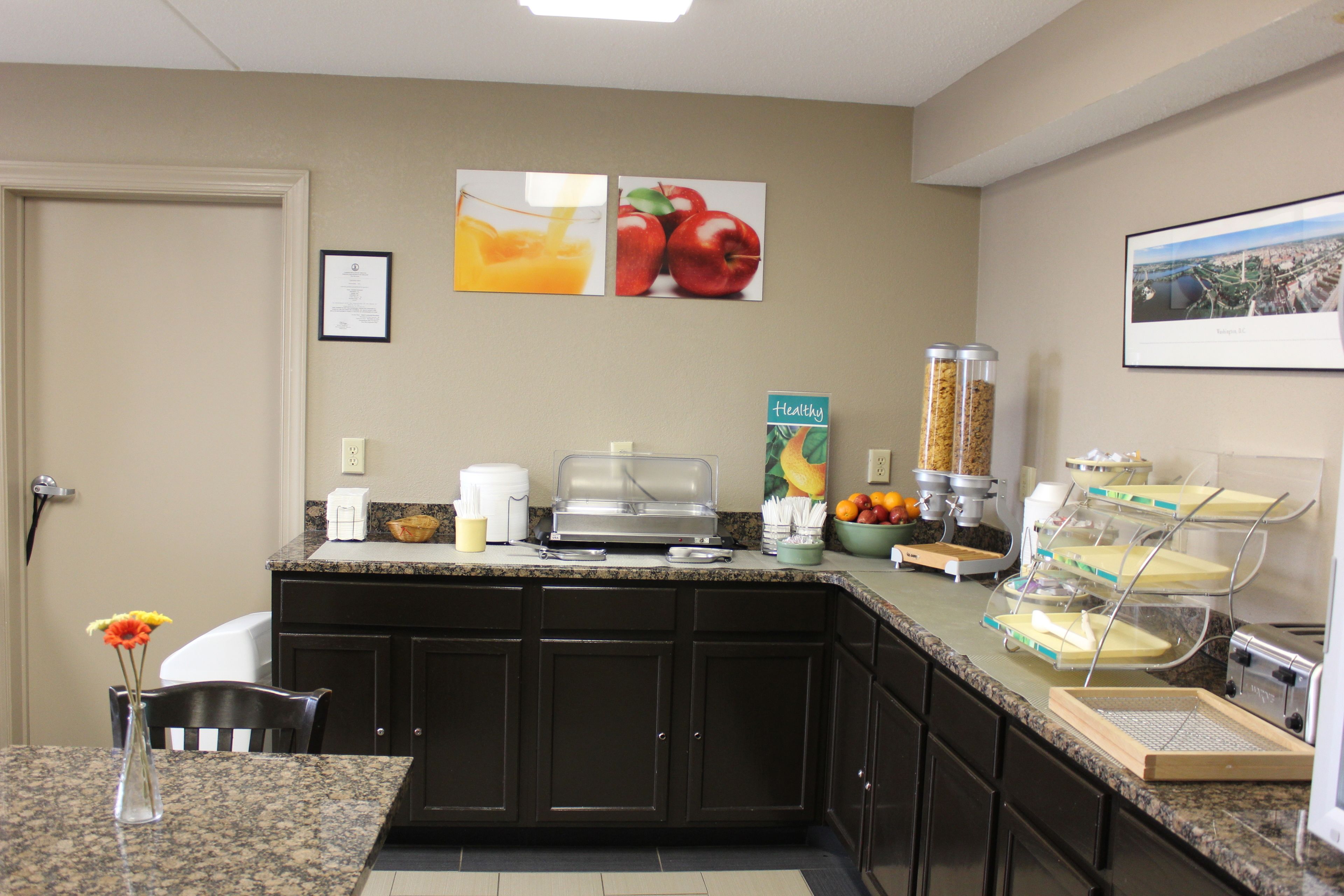Uma área de cozinha com serviço de buffet, incluindo cafeteira, tigela de frutas e dispensador de suco.