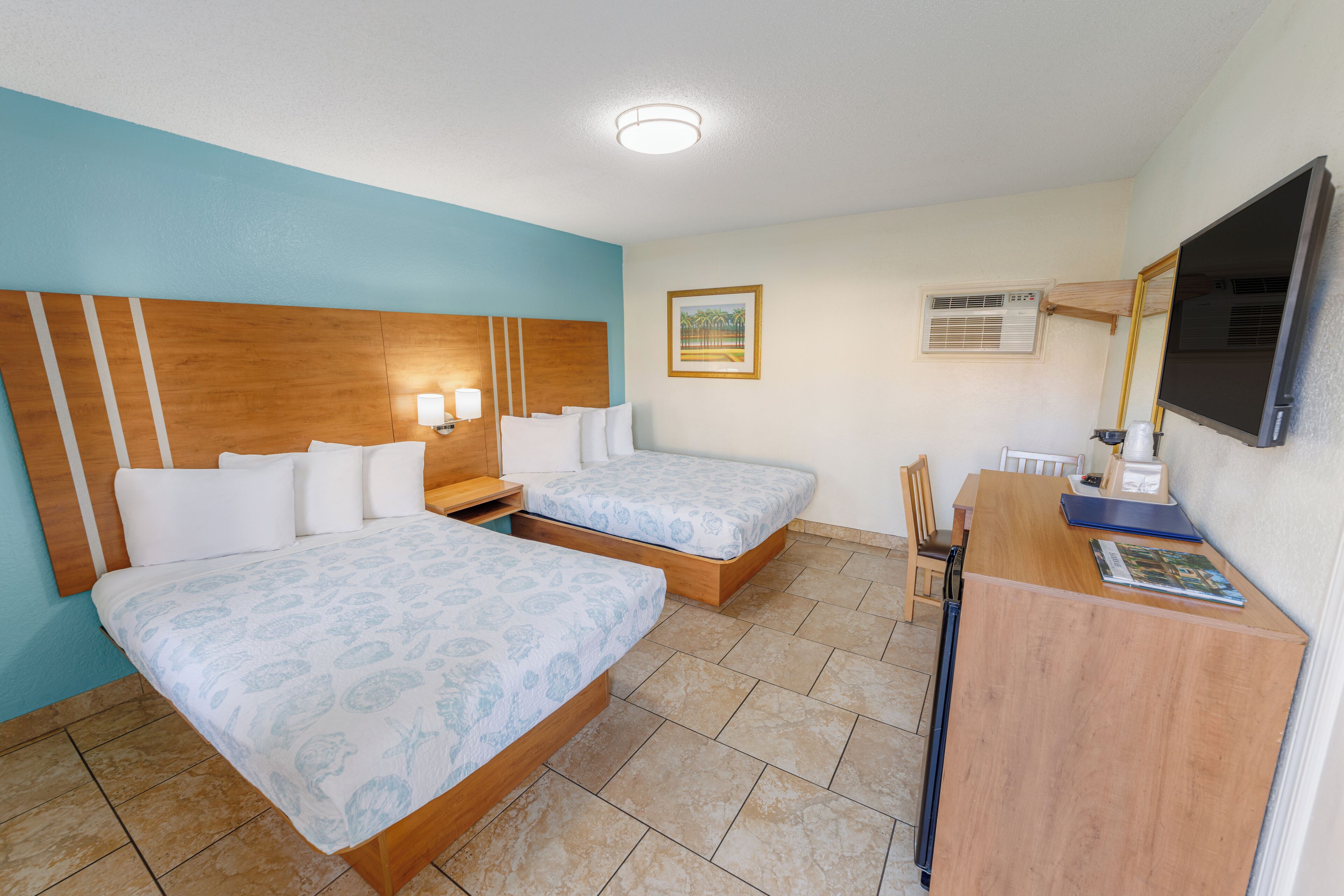 Quarto de hotel com duas camas, uma escrivaninha, uma cadeira, uma televisão e um aparelho de ar condicionado.