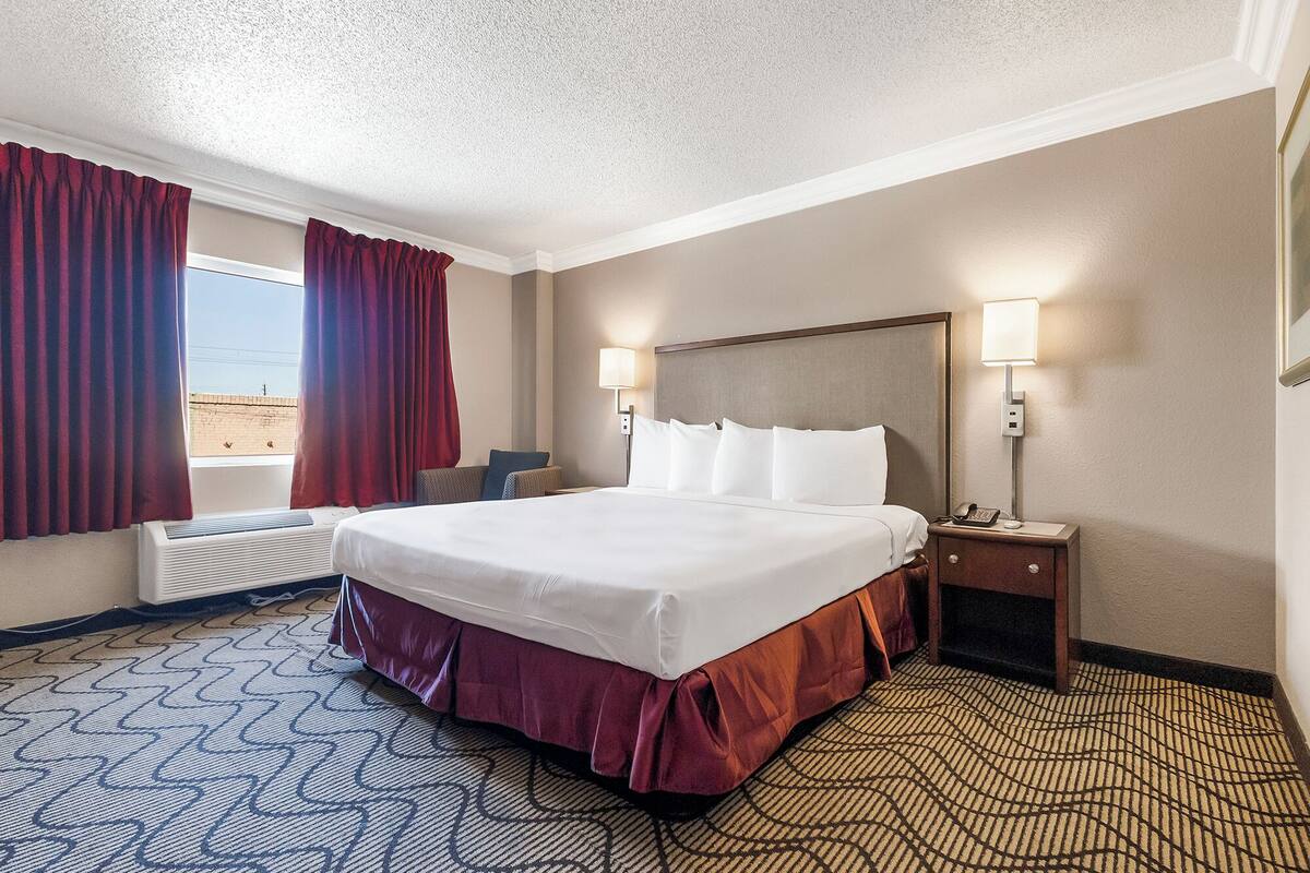 Quarto de hotel com uma cama grande, duas luminárias de cabeceira, um aquecedor e uma janela com cortinas.