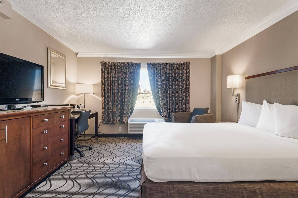 Quarto de hotel com cama, televisão, escrivaninha e uma cadeira.