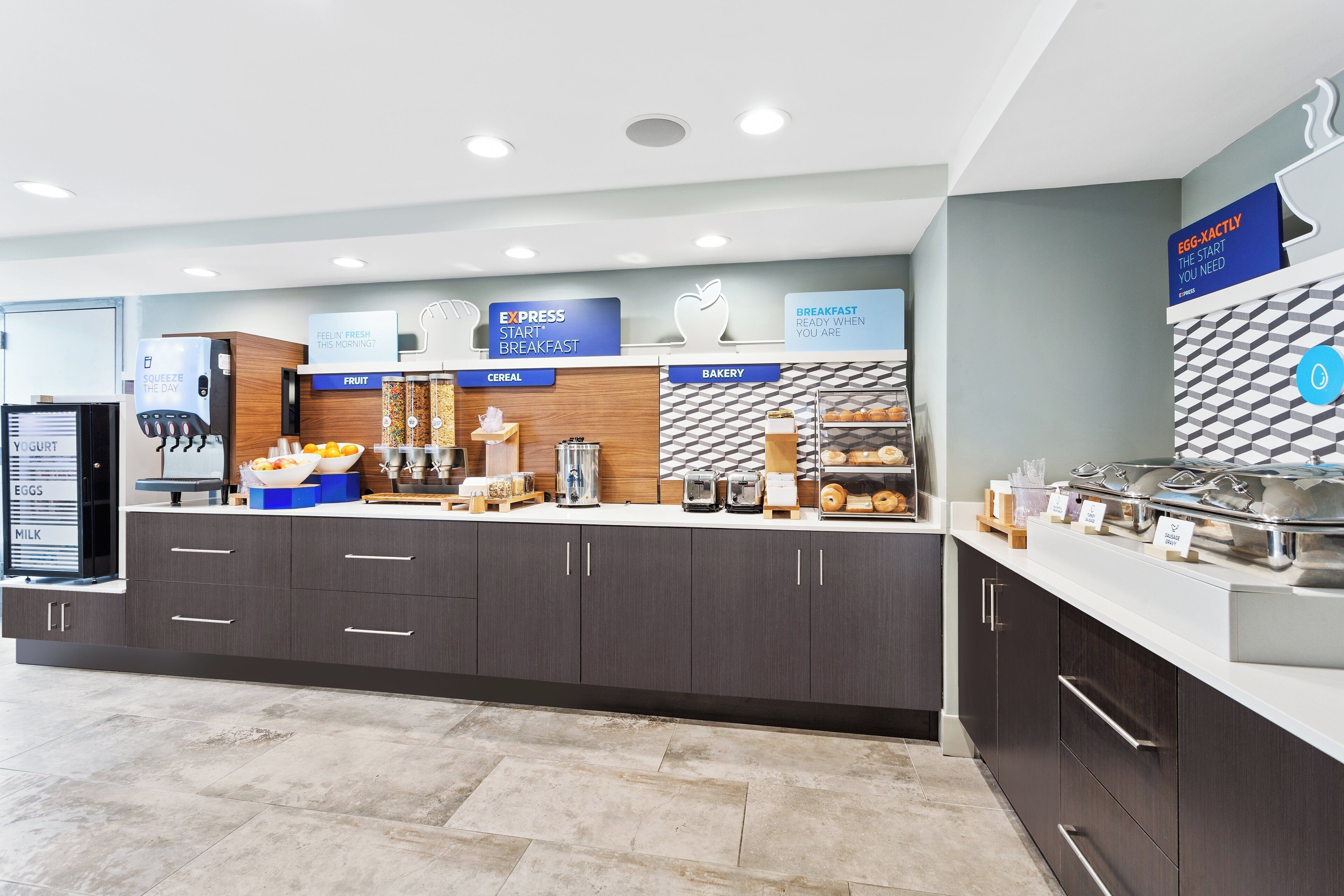 Espaço de café da manhã com estação de autoatendimento, incluindo dispensador de iogurte, cereais e produtos de panificação.