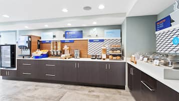 Espaço de café da manhã com estação de autoatendimento, incluindo dispensador de iogurte, cereais e produtos de panificação.