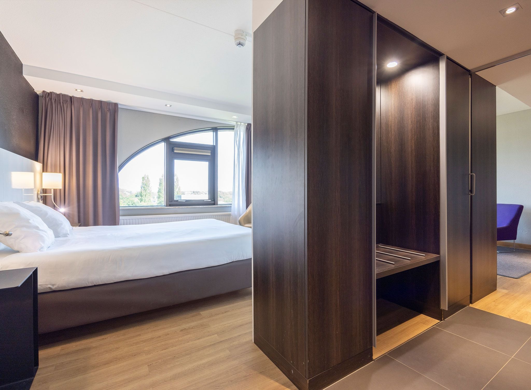 Quarto de hotel com cama, guarda-roupa e janela com cortinas.