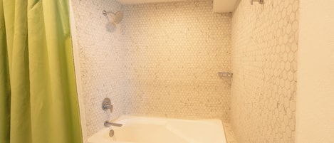 Um banheiro com parede de azulejos hexagonais, uma banheira branca e um cortina de chuveiro verde.